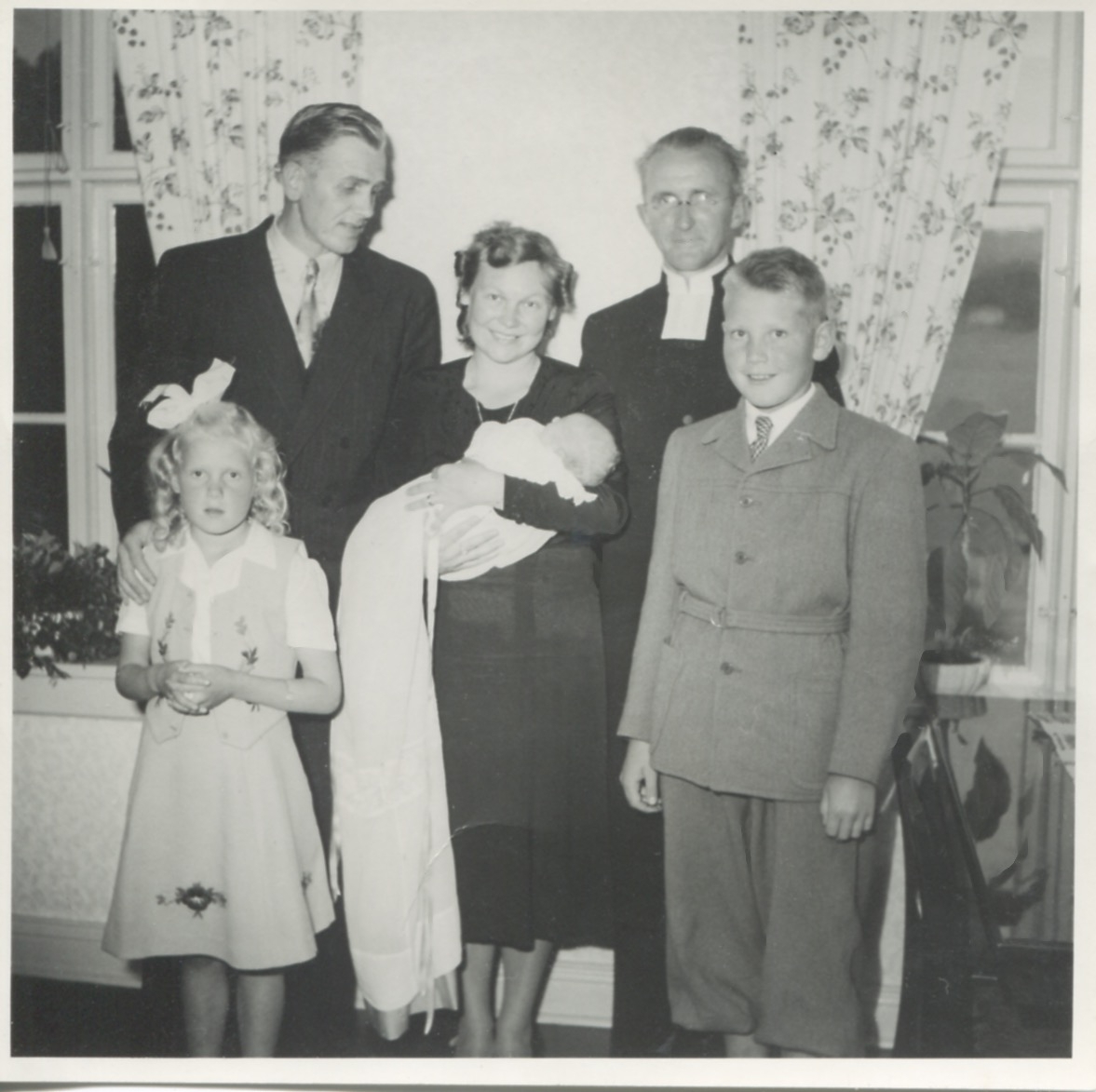 Dop av ett litet barn där familjen och prästen står samlade i ett rum ...