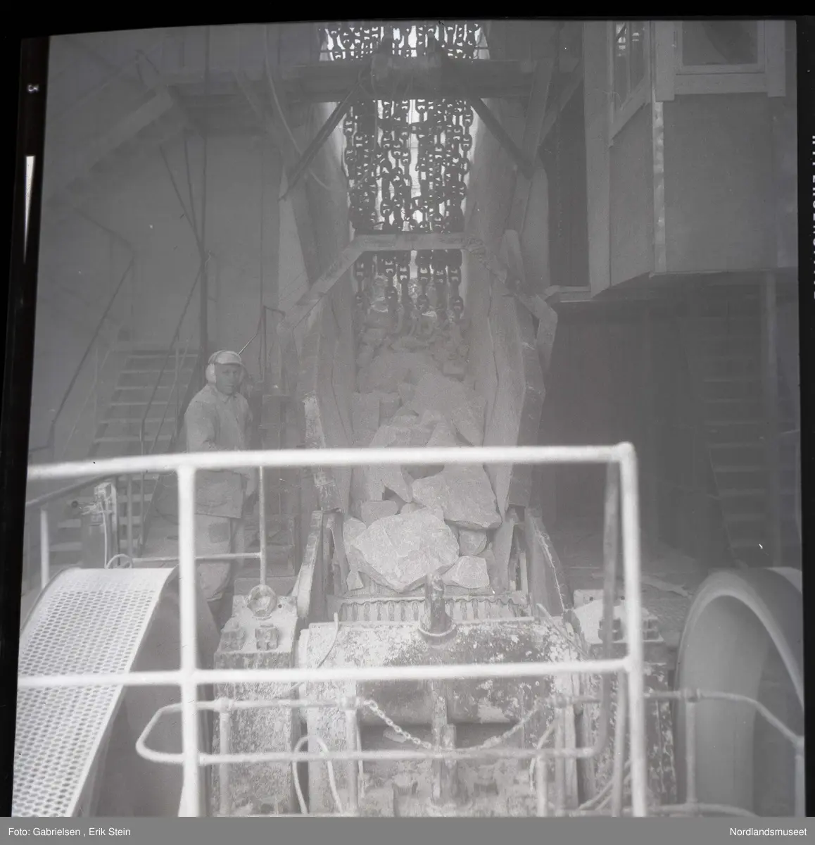 Fotografi av en arbeider kledd i arbeidsklær som står vedsiden av en ...