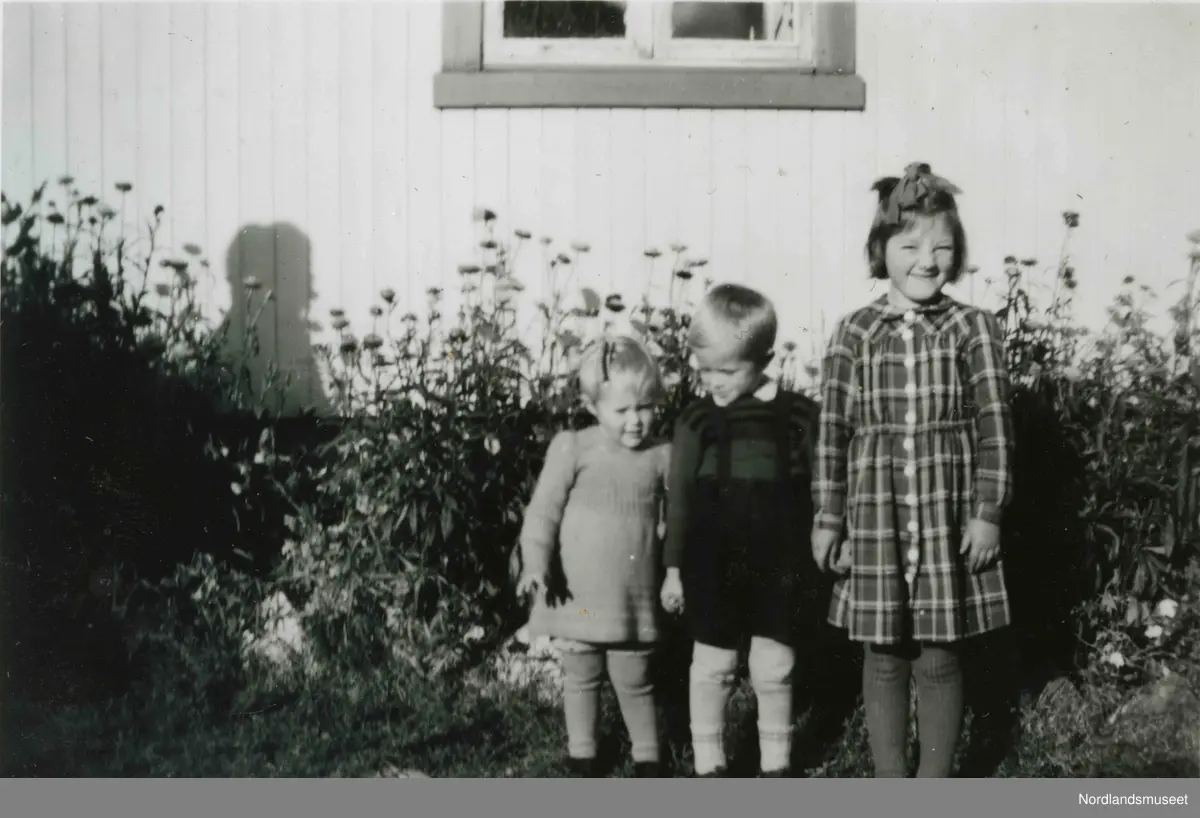 Tre små barn som står utenfor et hus. Blomsterbed. - Nordlandsmuseet ...