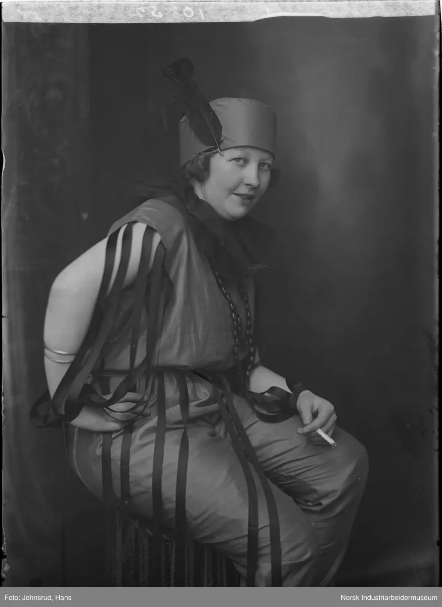 Kvinne stående oppstilt i kostyme. Kvinnen har ett ben på en stol med ...