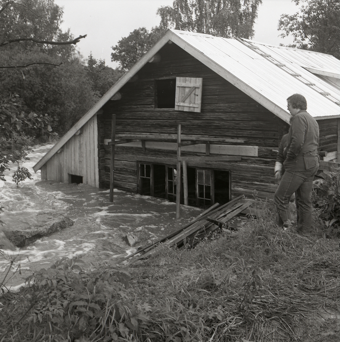 Två män betraktar en översvämmad byggnad där halva huset står under ...