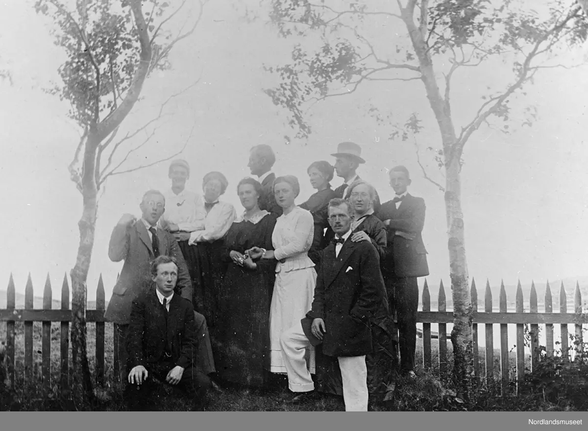 En gruppe mennesker samlet foran et gjerde med to trær, ett tre på hver ...