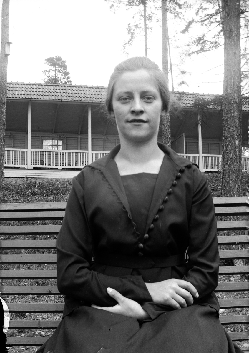 En kvinna, Ebba Berg, sitter på en bänk med en träveranda i bakgrunden ...